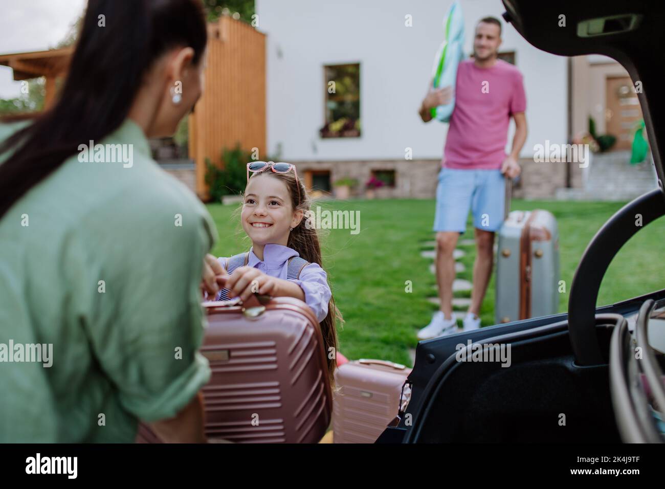 Happy family preparing for holiday, putting suitcases in car trunk ...