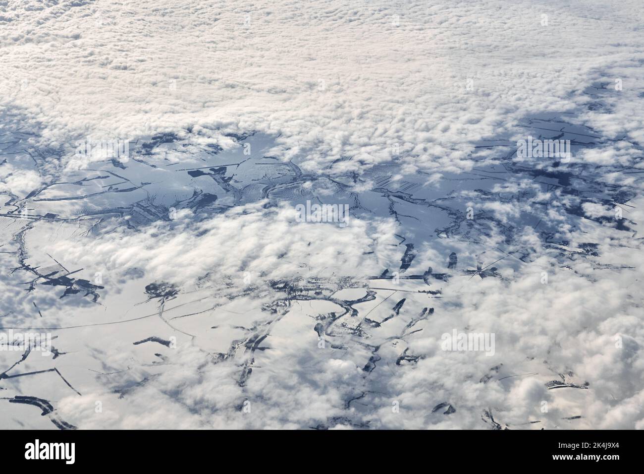 Aerial cloudscape view over top clouds to snow covered rivers, roads ...