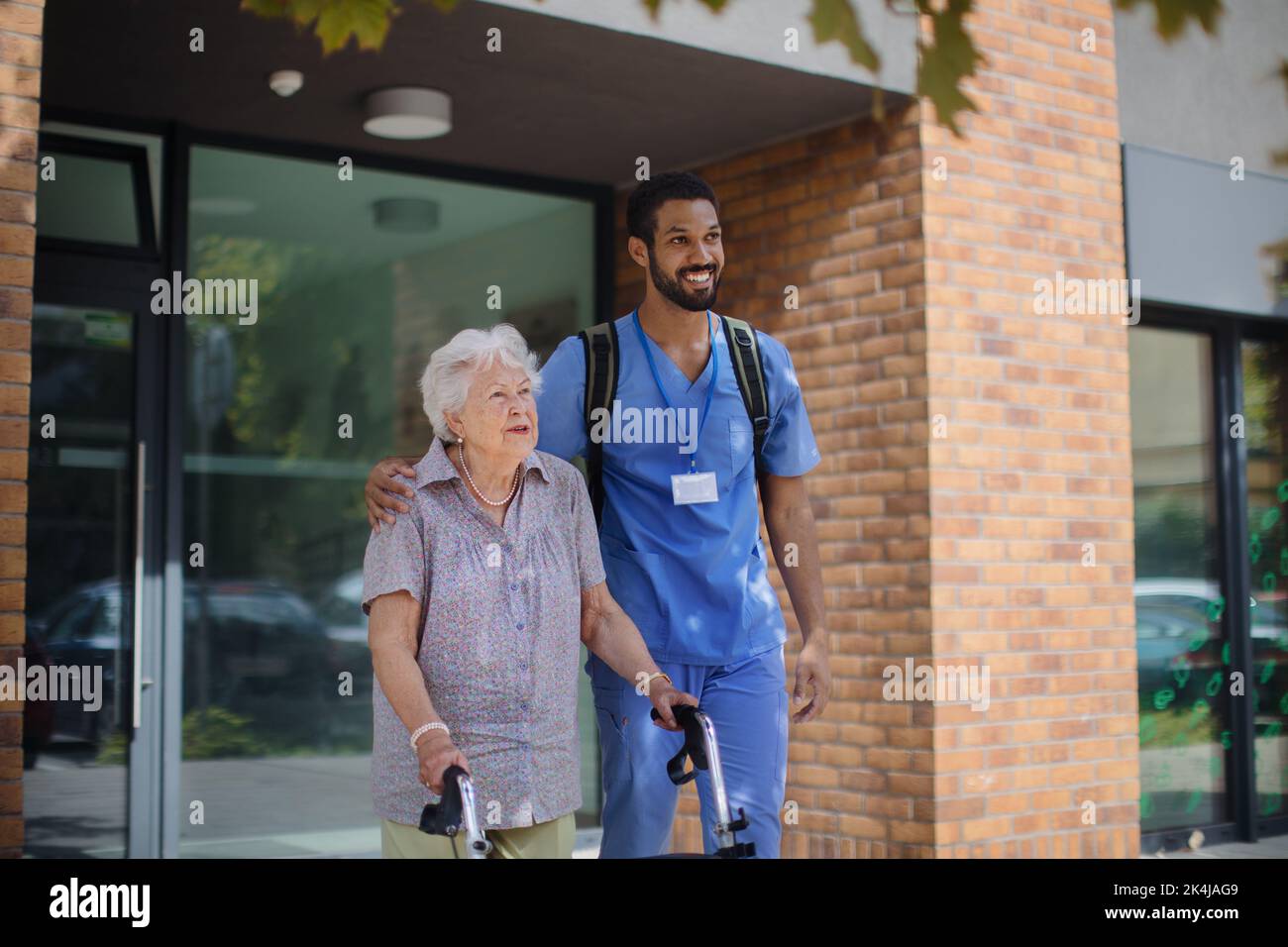 Caregiver walking with senior woman client in front of nurishing home ...