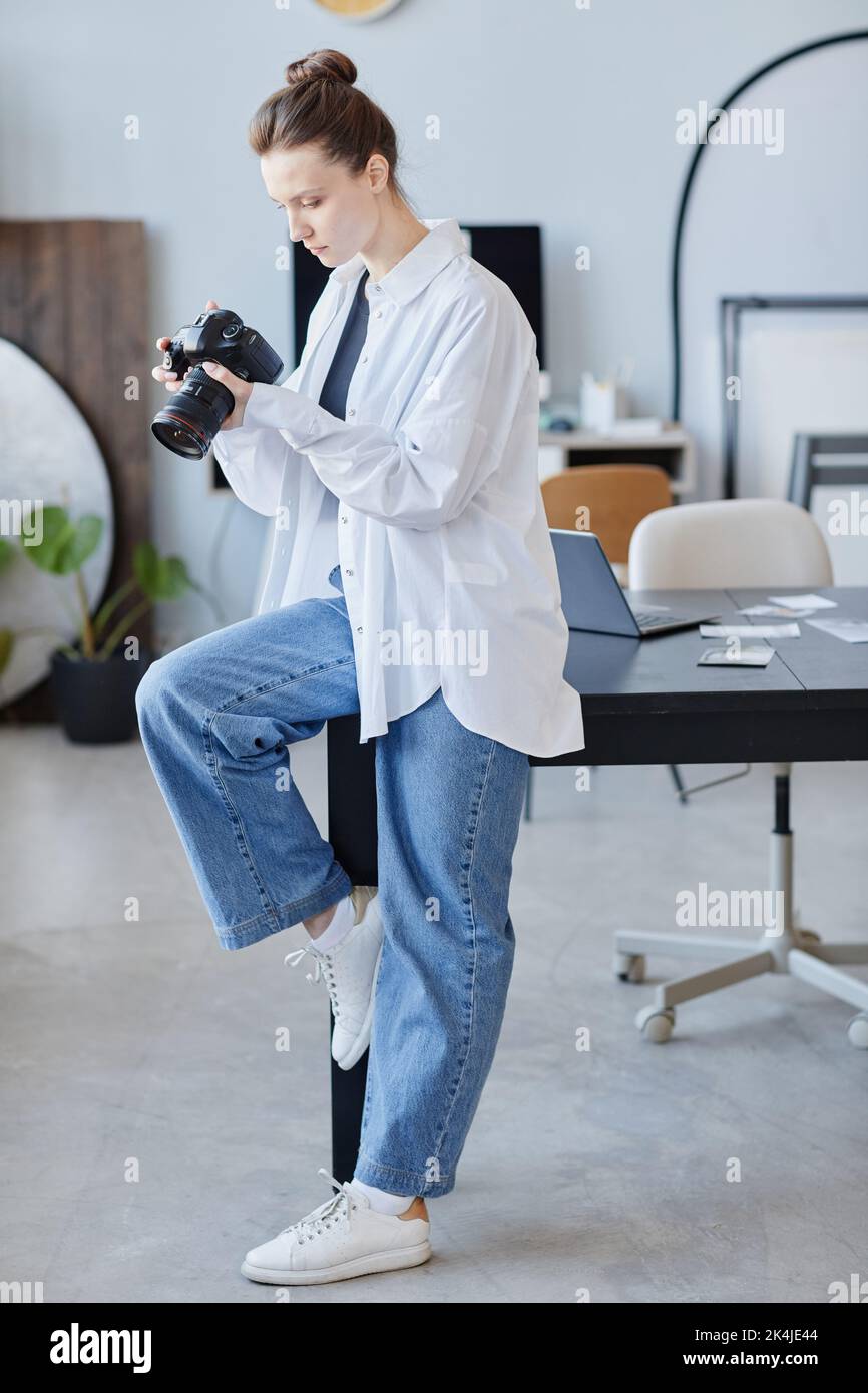 Vertical full length portrait of female photographer checking images in ...