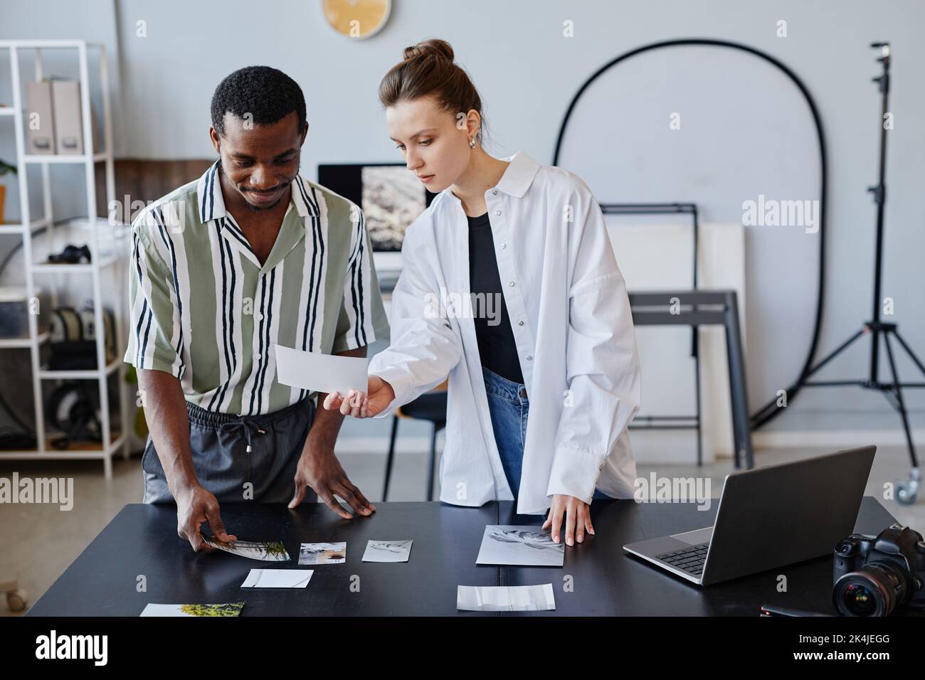 Portrait of two photographers laying out printed images on table and ...
