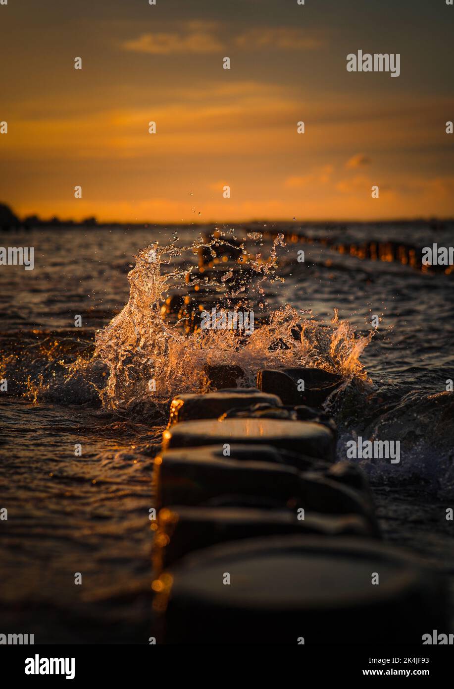 Golden Water splashing on a stone pier line in the beach in the sea at ...