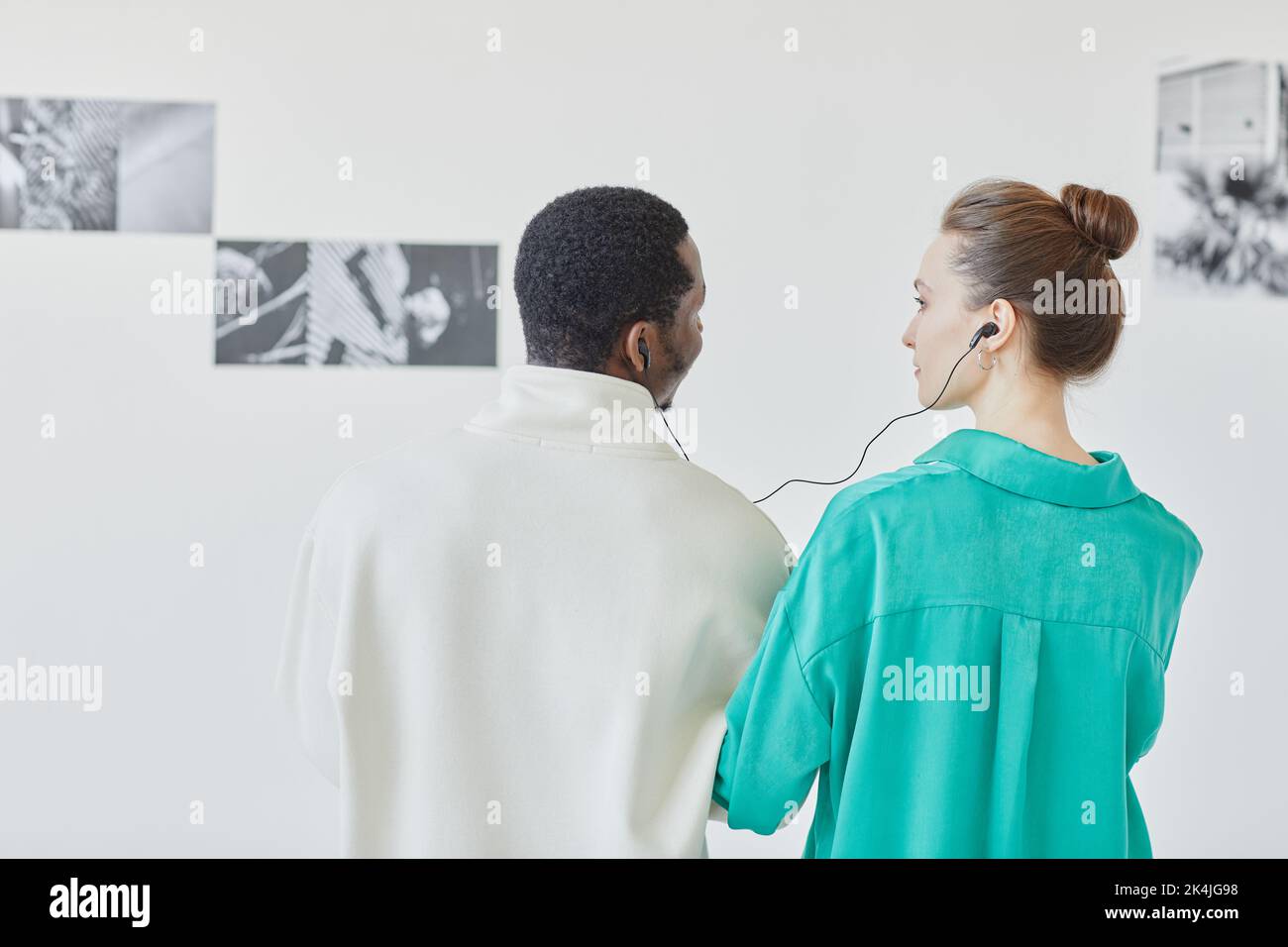 Minimal back view of young couple with earphones looking at abstract ...