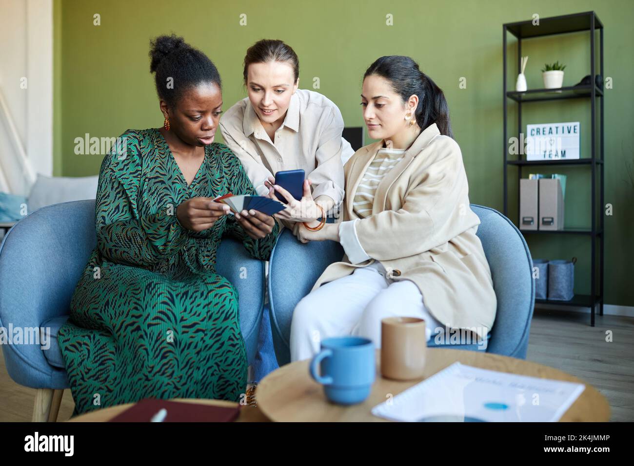 Three young intercultural female designers discussing color palette at ...