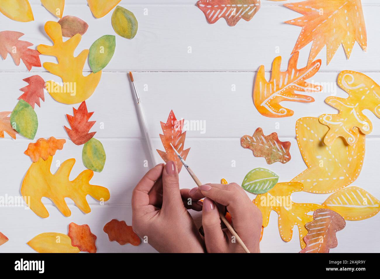 Female hand drawing autumn leaves of different shapes, sizes and colors ...