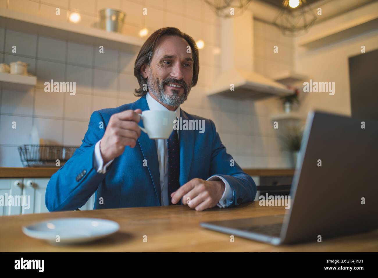 Man in blue suit having a vieo call and looking contented Stock Photo ...