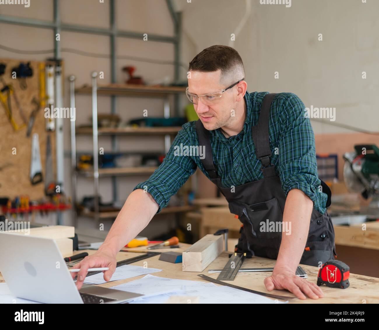 Portrait of a carpenter in protective glasses and work overalls uses a ...
