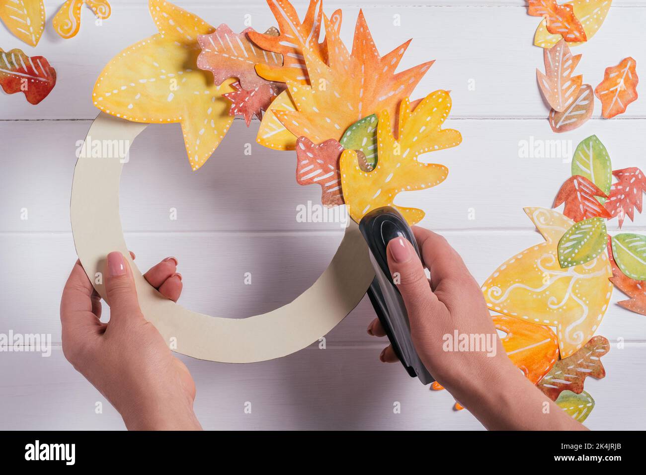 Female hands making decorative autumn paper wreath. Using stapler to ...
