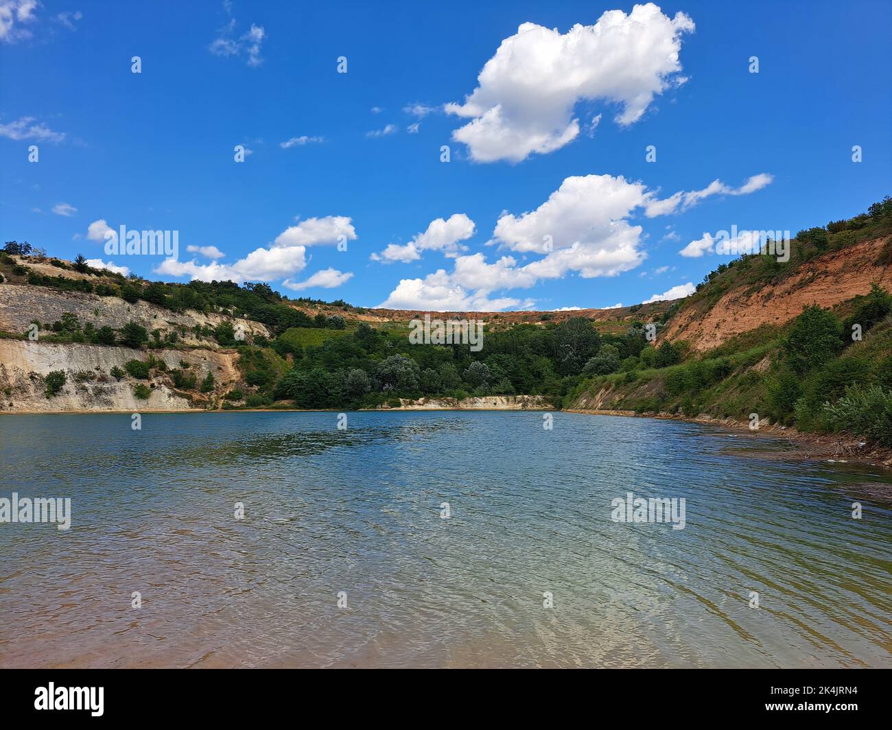 A lake surrounded by cliffs and trees under a blue sky Stock Photo - Alamy