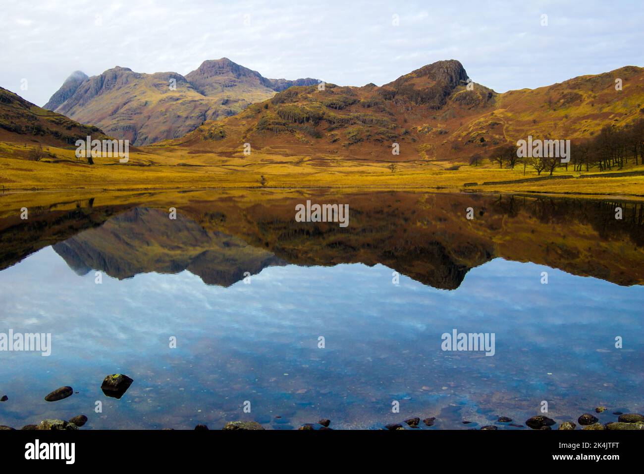 The reflections of the Langdale Pikes mountains in the still water of ...