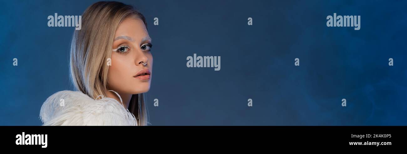 pierced woman with winter makeup and frozen eyebrows posing on dark ...