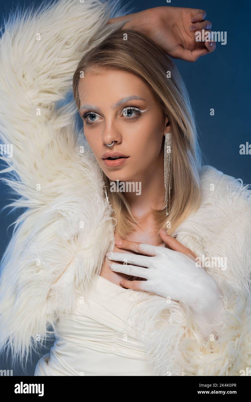 pierced young woman with winter makeup posing in white jacket with ...
