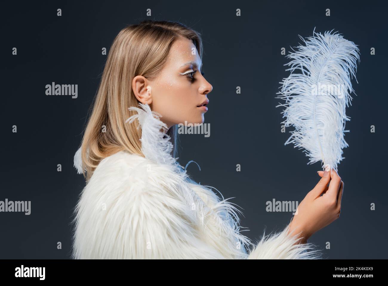 side view of blonde woman with winter makeup looking at feather ...