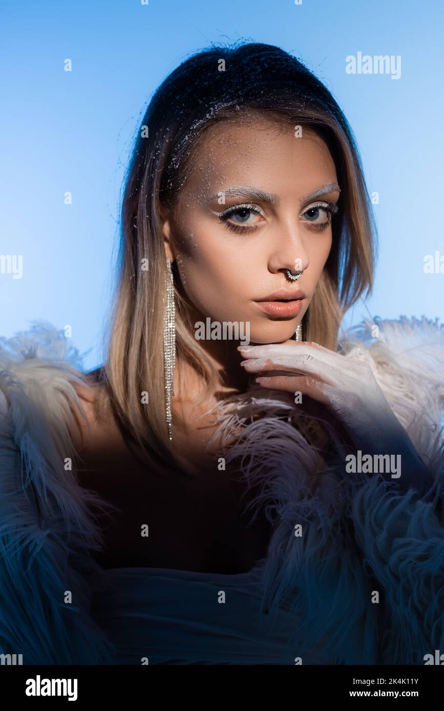 young blonde woman with snowy eyebrows in jacket with feathers looking ...