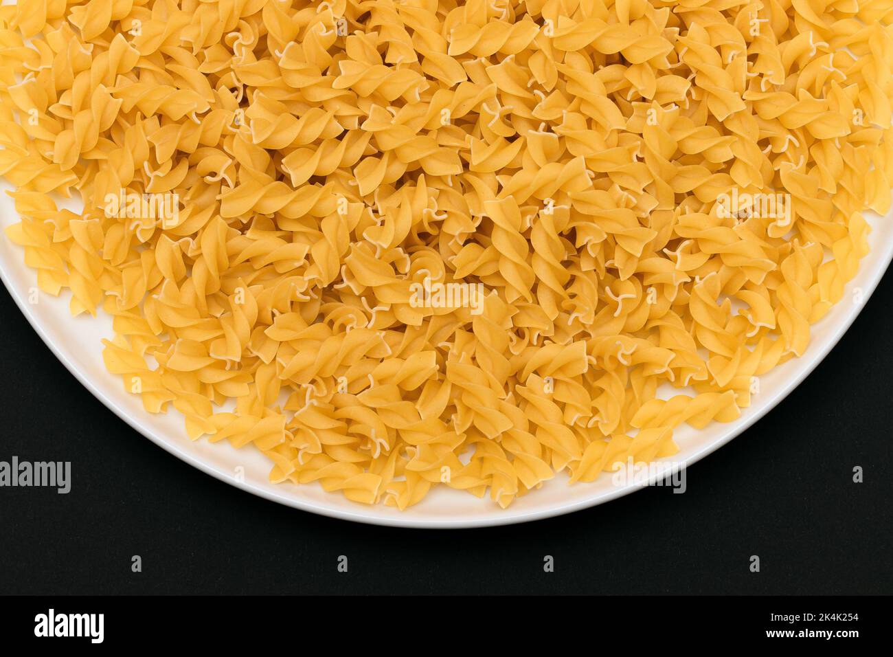 Uncooked Fusilli Pasta Lying on White Plate on Black Background. Raw ...