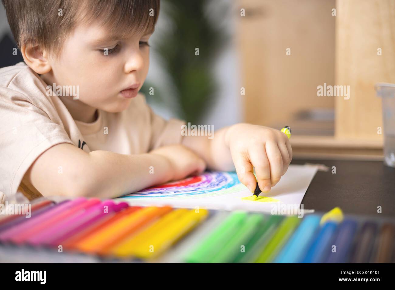 Enthusiastic male kid drawing multicolor rainbow paper sheet closeup ...