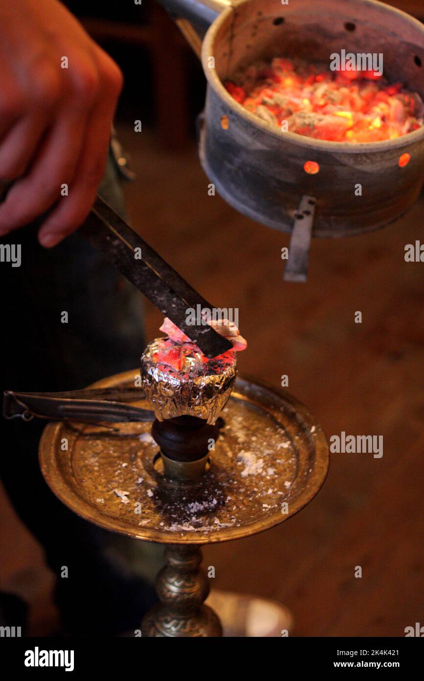 Using tongs to place red hot charcoal, coals, on a hookah, shisha ...