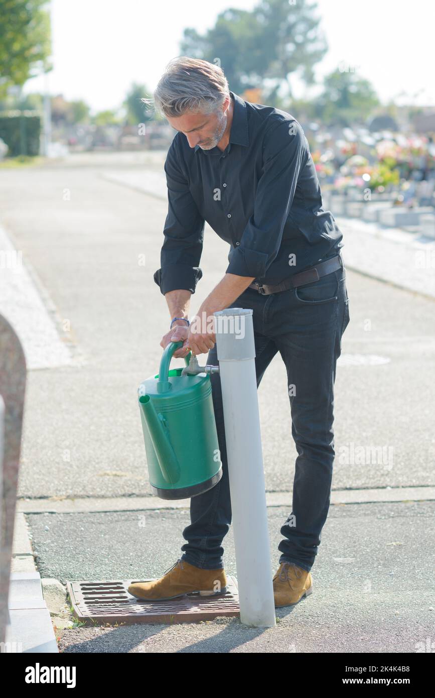 Man filling watering can in cemetary Stock Photo - Alamy