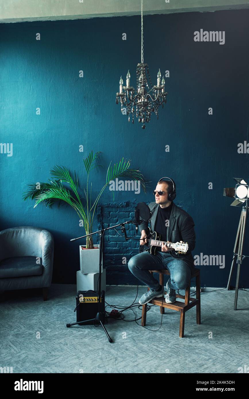 Man singer sitting on a stool in a headphones with a guitar recording a ...