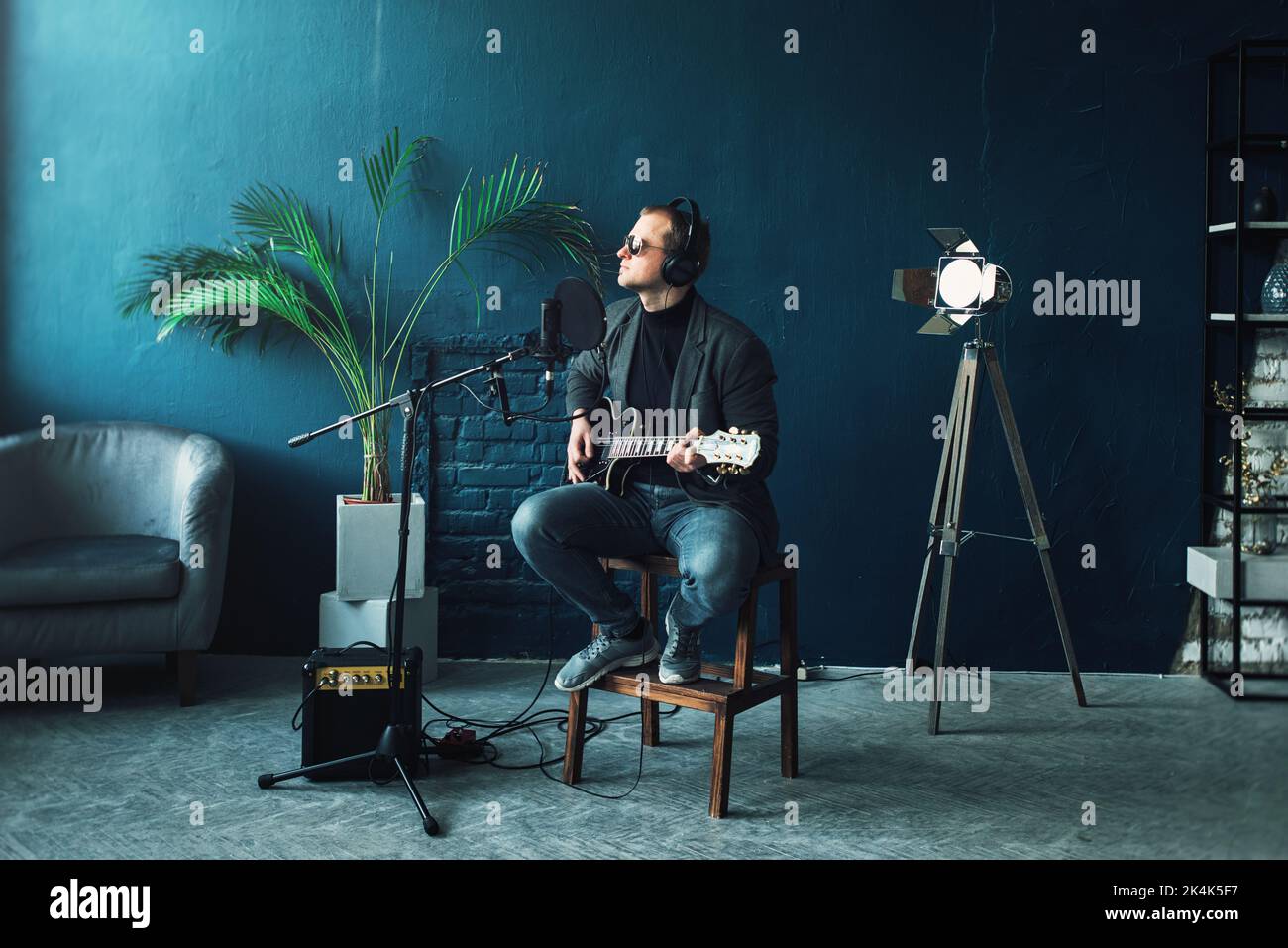 Man singer sitting on a stool in a headphones with a guitar recording a ...