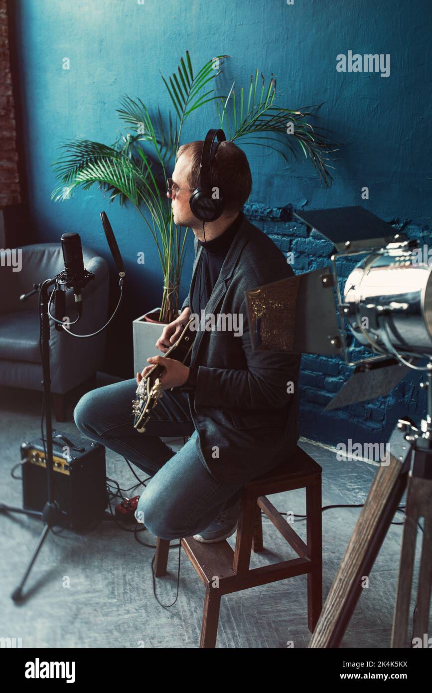 Man singer sitting on a stool in a headphones with a guitar recording a ...