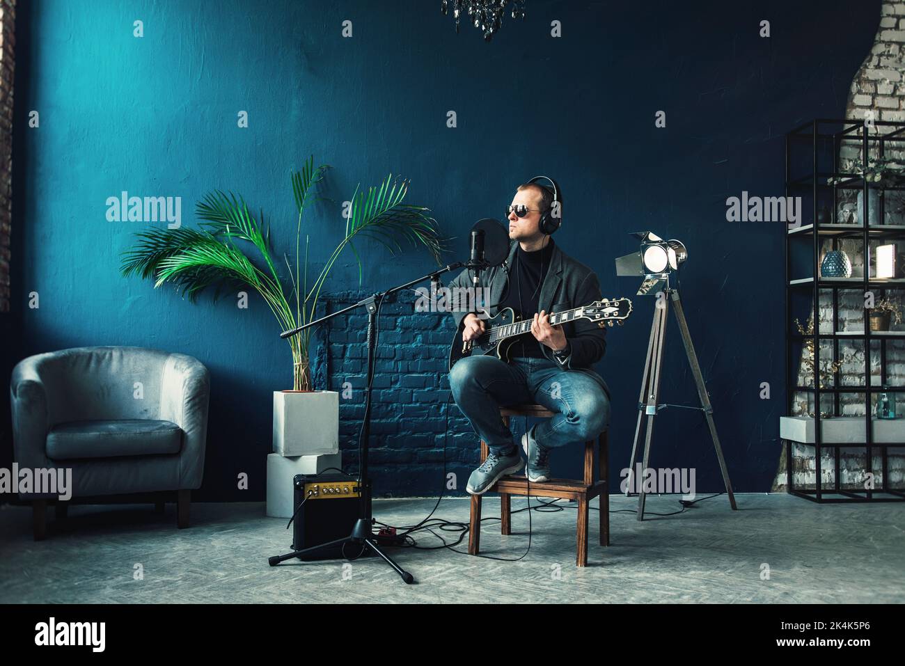 Man singer sitting on a stool in a headphones with a guitar recording a ...
