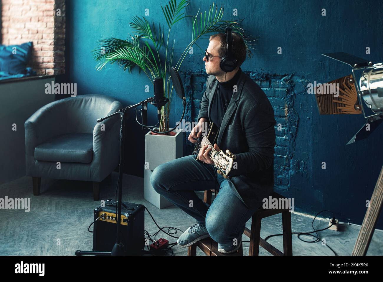 Man singer sitting on a stool in a headphones with a guitar recording a ...
