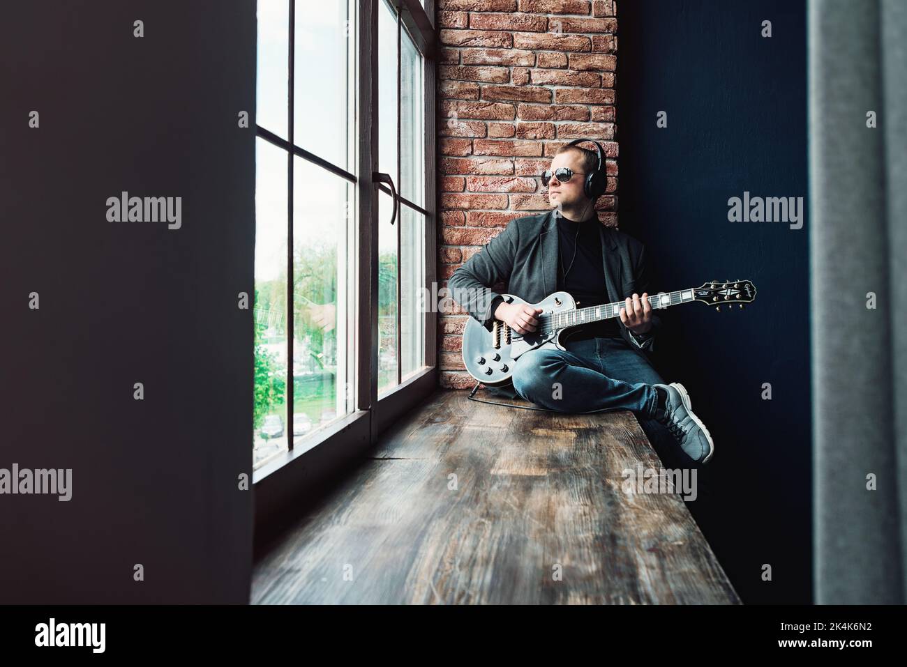 Man singer sitting on a window sill in a headphones with a guitar ...