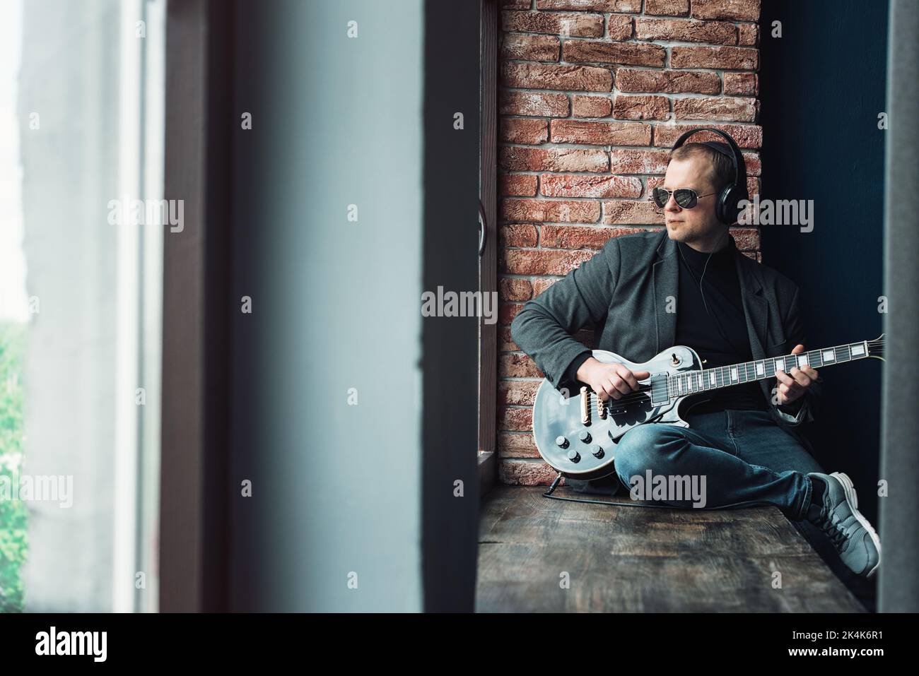 Man singer sitting on a window sill in a headphones with a guitar ...