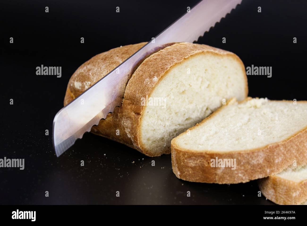 Close up large knife cuts thin pieces of white bread from a rectangular ...