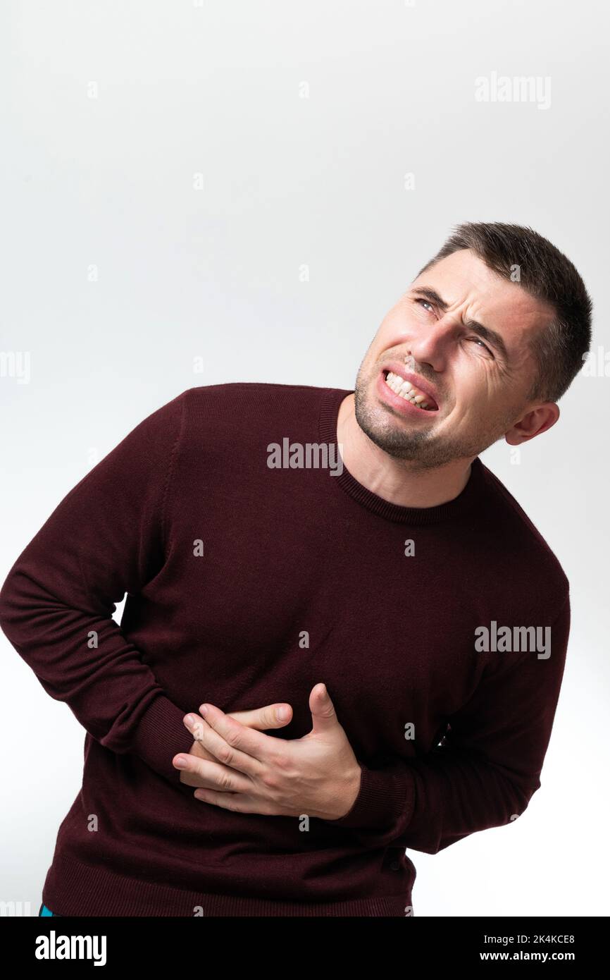 A man touches his stomach with two hands, on a white background with ...