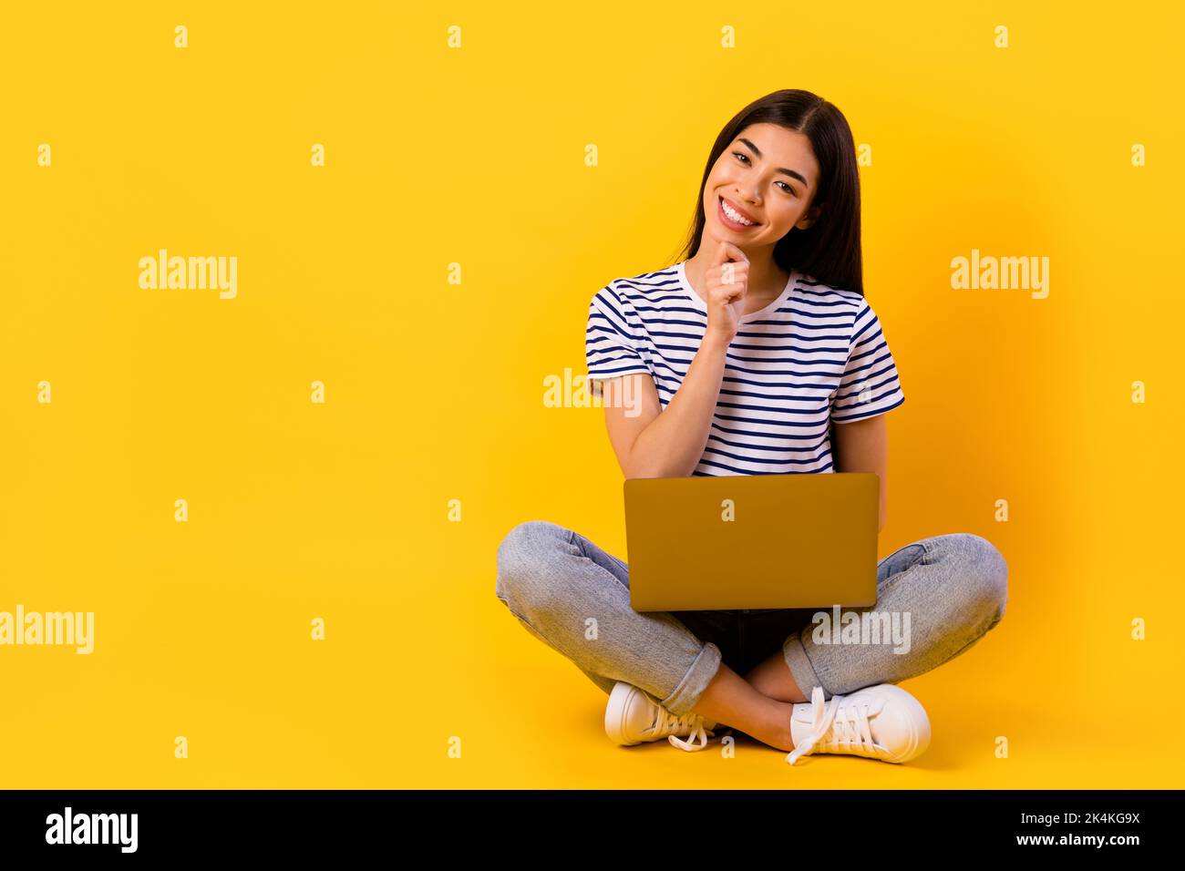 Full length photo of positive nice thai person sit floor arm touch chin ...
