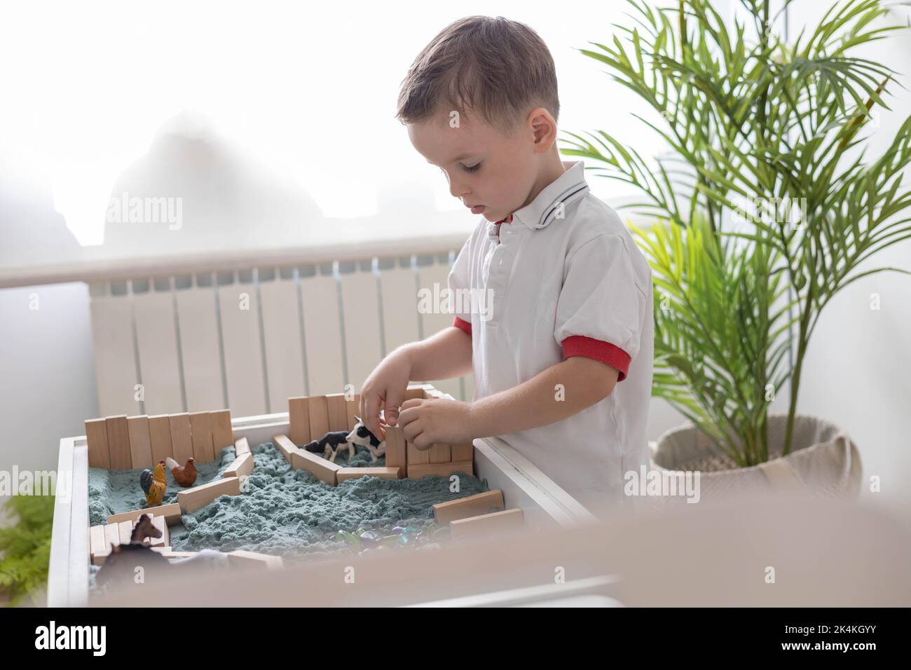 Cute baby boy playing sensory box kinetic sand table with farm animals ...