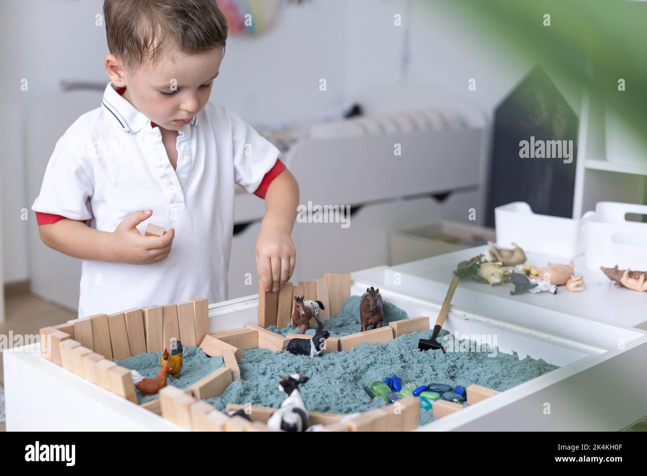 Cute baby boy playing sensory box kinetic sand table with farm animals ...
