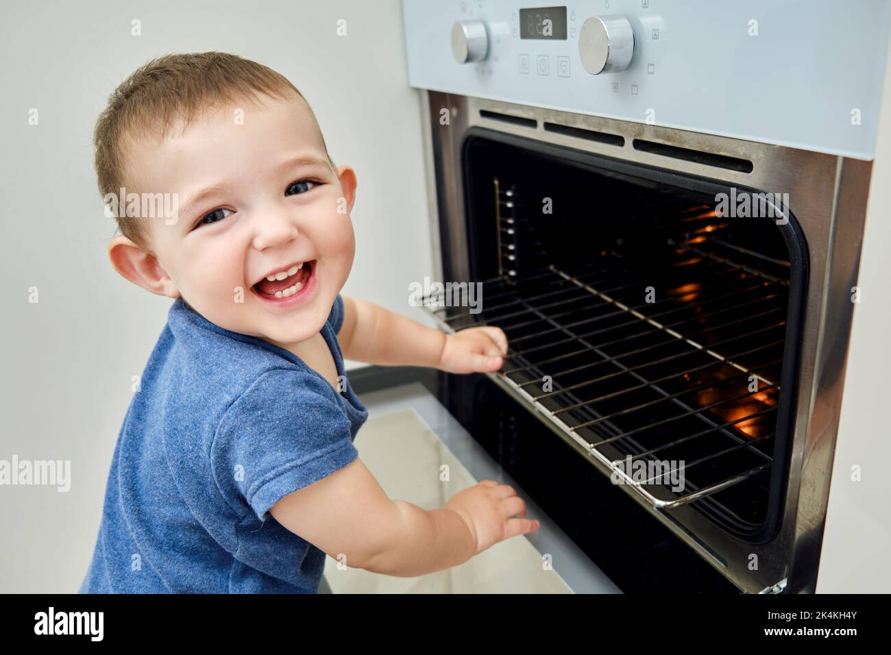 Toddler baby climbs into a hot electric oven. Child boy opens oven door ...