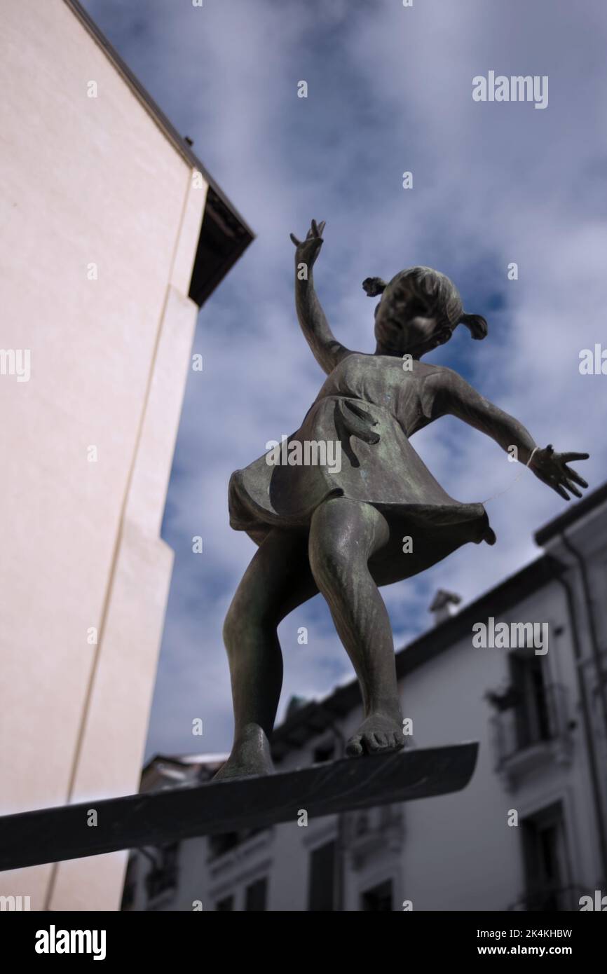 A vertical low angle of a girl statue trying to keep her balance to not ...