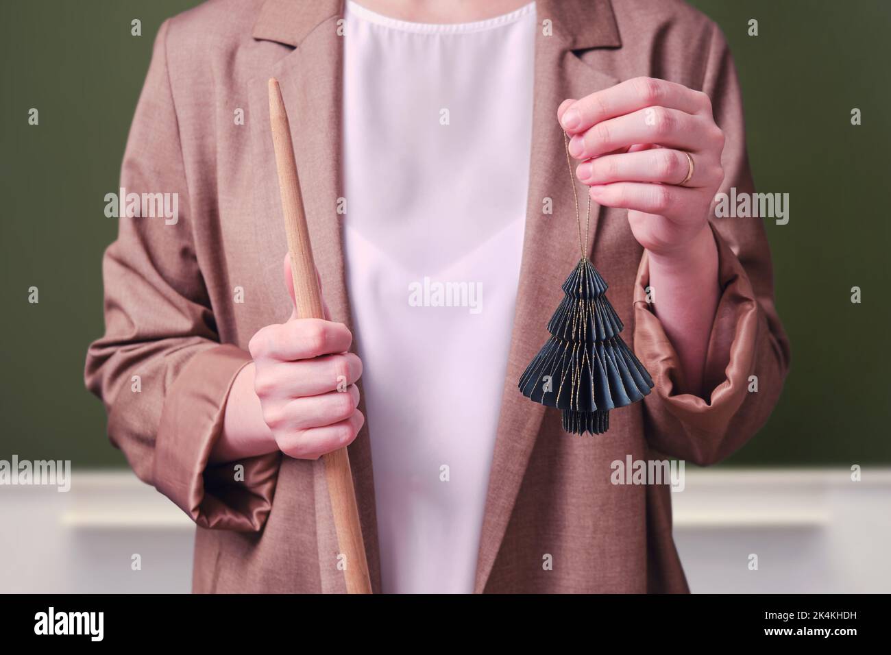Woman teacher holding a decorative christmas toy in her hands on a school blackboard in the ...