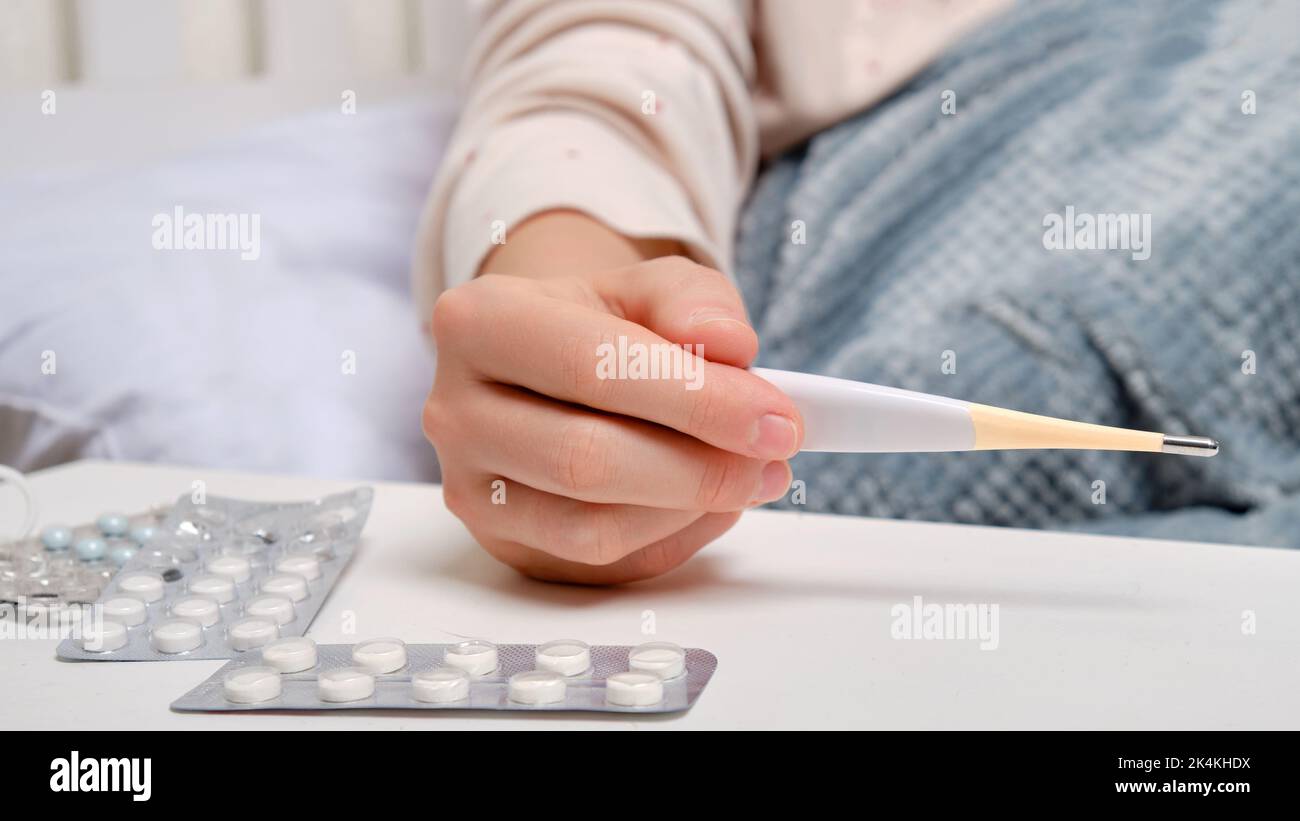 A sick woman looks at a thermometer in her hand in her hand, fever and ...
