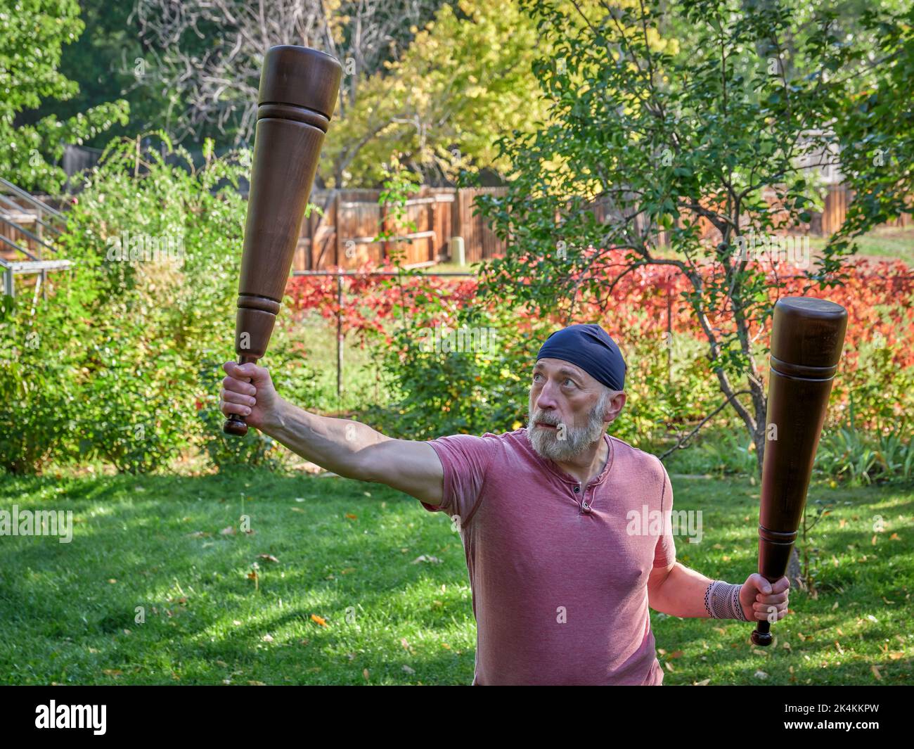 senior man (late 60s) is exercising with heavy wooden Persian meels in ...
