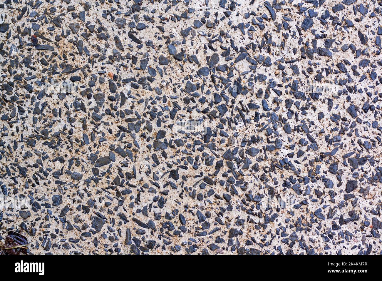 Old concrete wall interspersed with black small pebbles. Horizontal ...