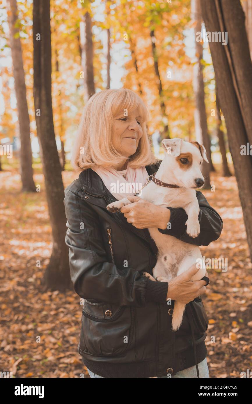 Senior smiling woman hugging her dog in autumn park. Active aging and ...