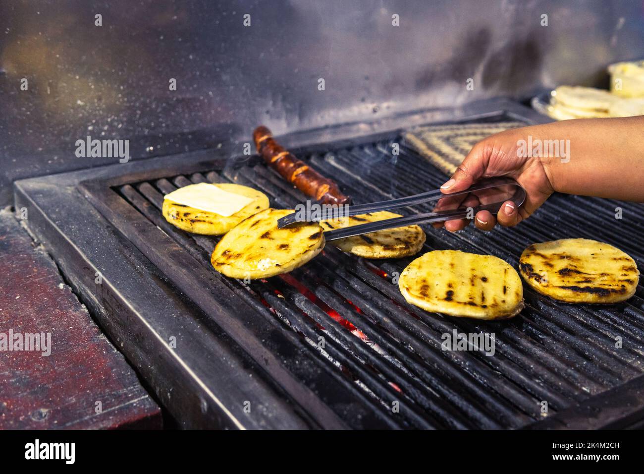 Close-up of a hand grilling arepas and chorizo over charcoal ...