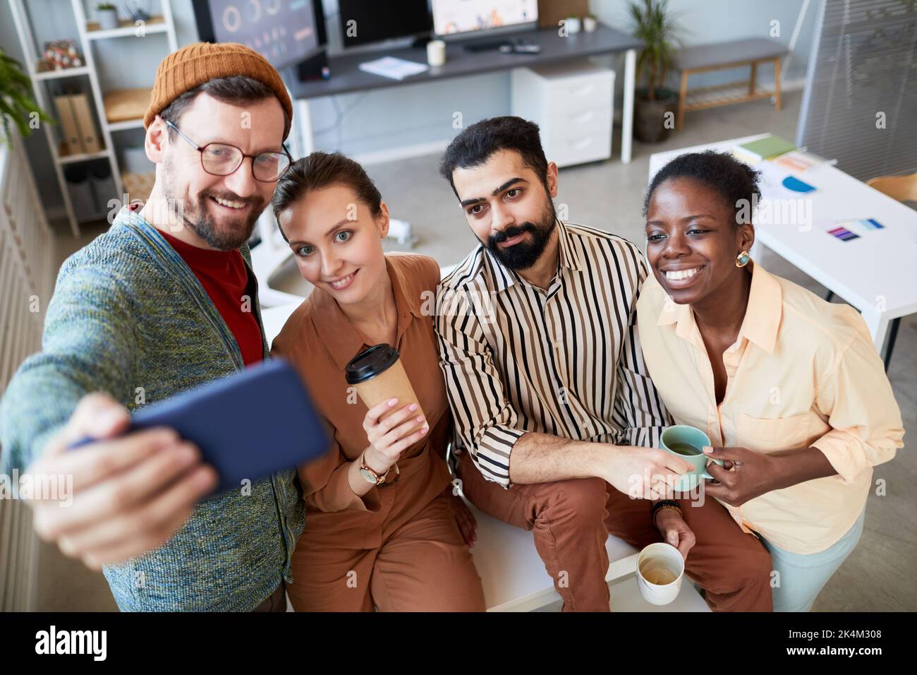 Group of four young multicultural coworkers with cups of coffee and tea ...