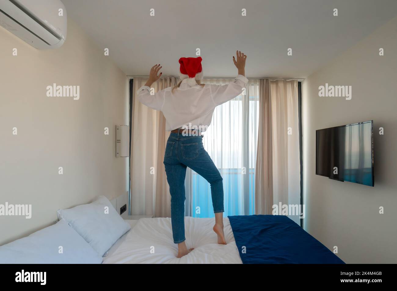 Happy young woman in blue jeans, a white shirt, a Santa Claus hat jumps ...