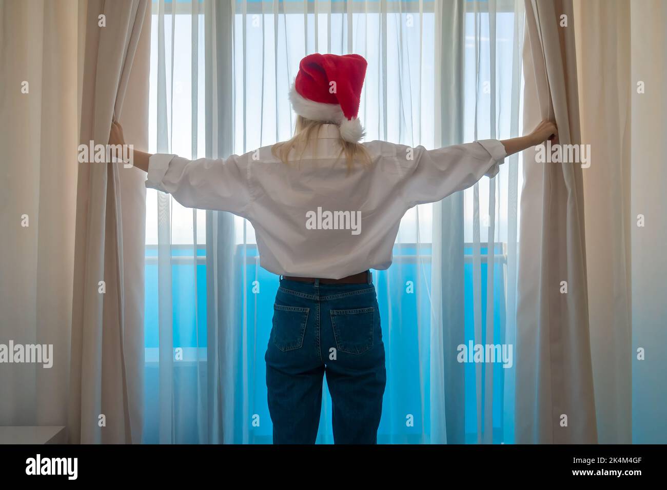 Young woman in a Santa Claus hat in a white shirt and blue jeans opens ...