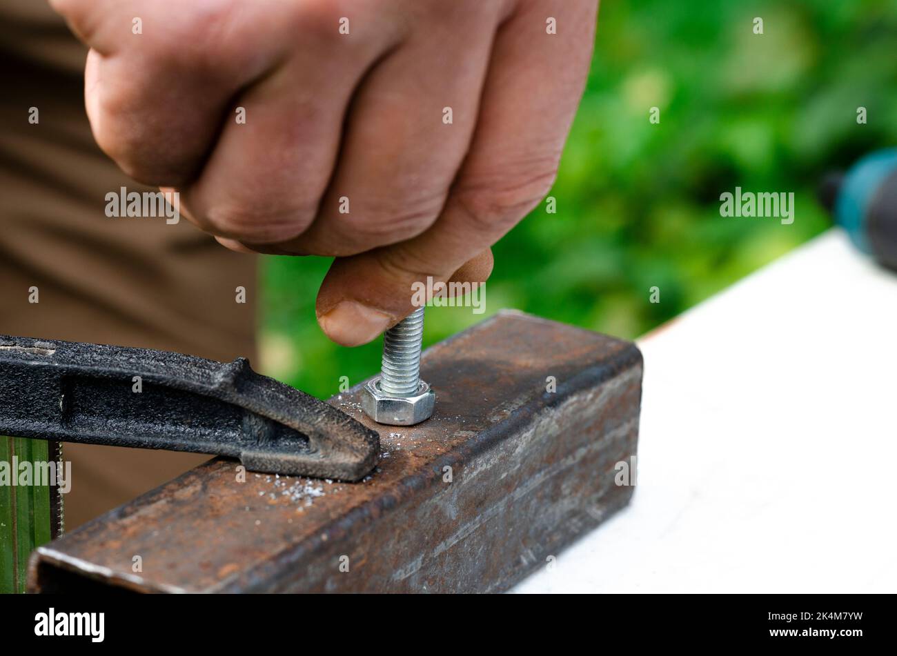 A man's hand screws a bolt into a metal nut. Working with metal Stock ...