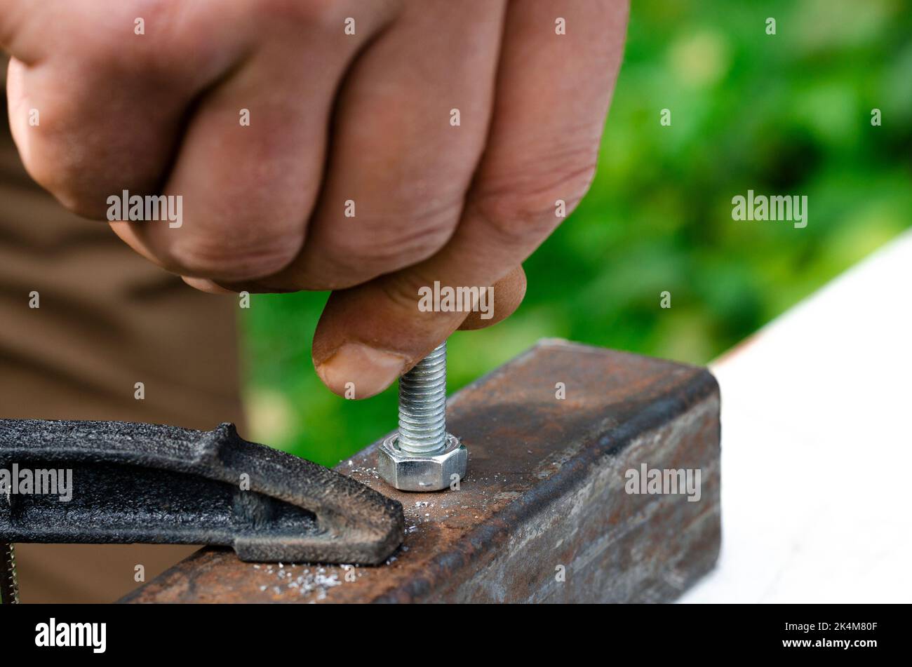 A man's hand screws a bolt into a metal nut. Working with metal Stock ...