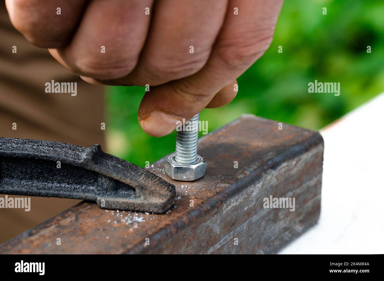 A man's hand screws a bolt into a metal nut. Working with metal Stock ...