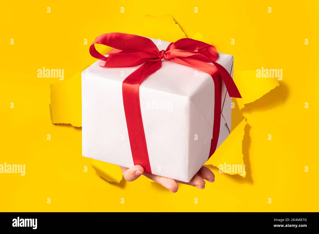 Hand giving gift box through torn yellow paper background, closeup ...