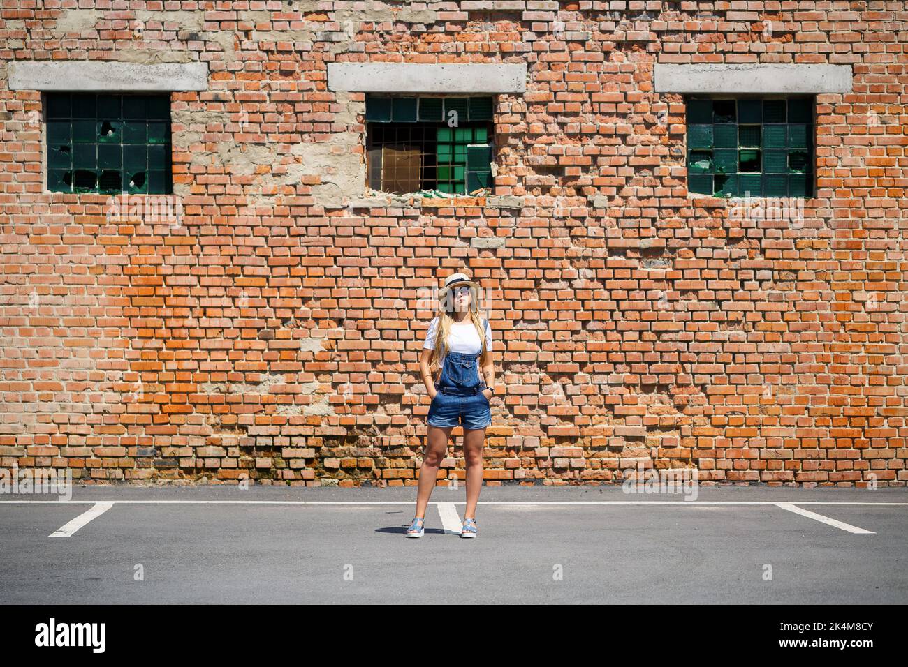 Girl in denim overalls, a white T-shirt and a light hat on a background ...